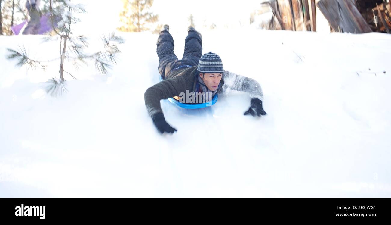 Man sliding down snowy hill in sled Stock Photo - Alamy