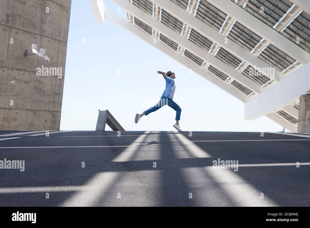 Woman with ponytail jumping in joy and raising arms in urban outside ...