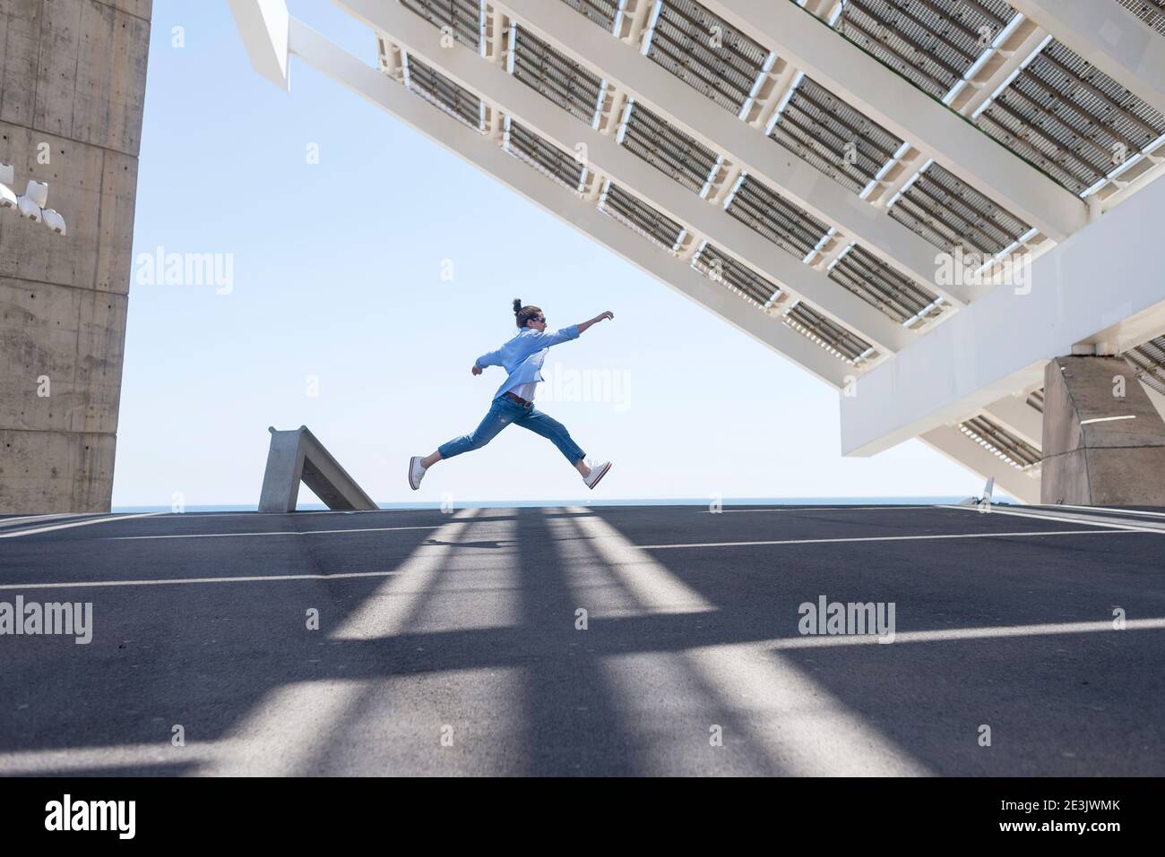 Woman with ponytail jumping in joy and raising arms in urban outside ...