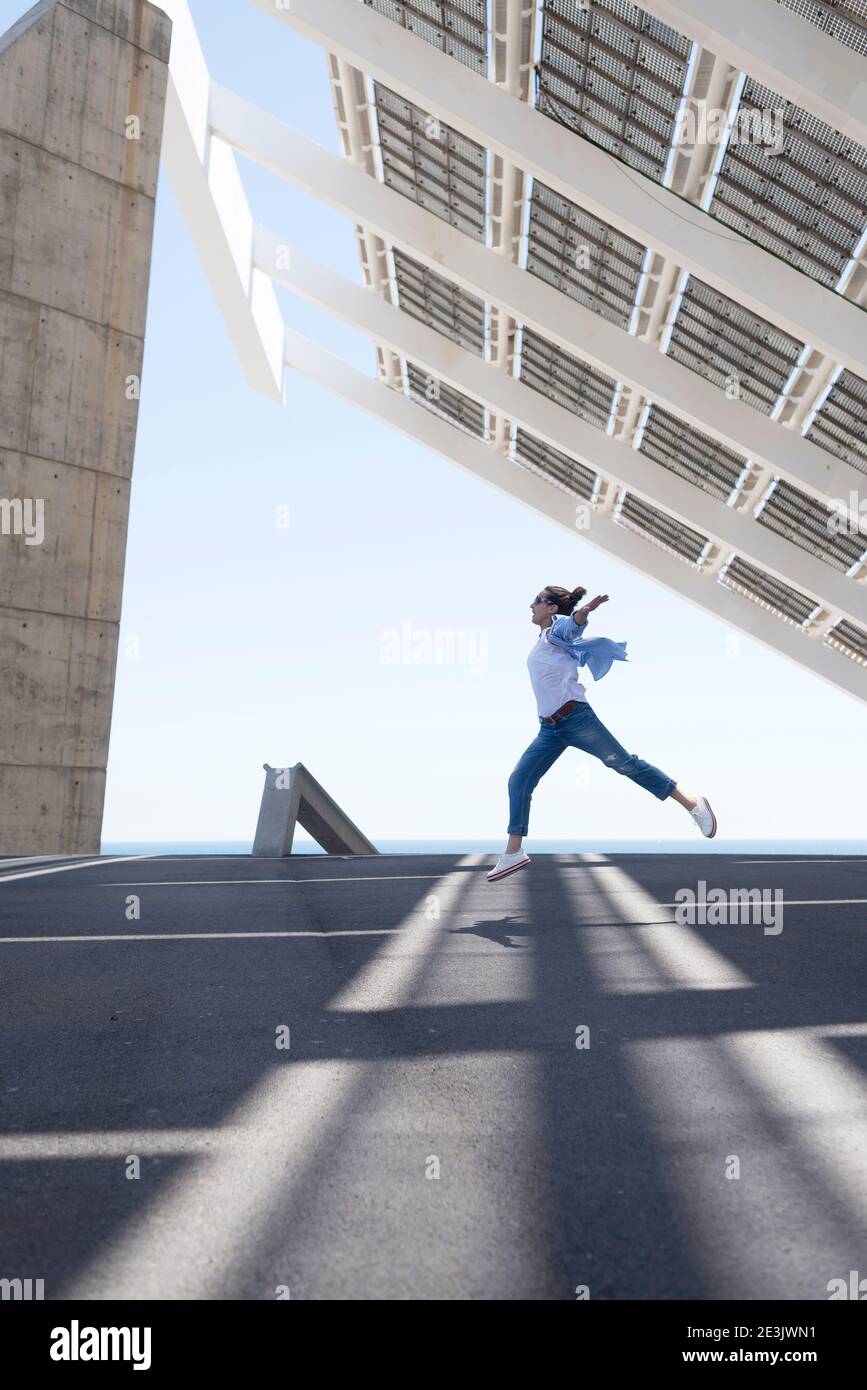 Woman with ponytail jumping in joy and raising arms in urban outside ...