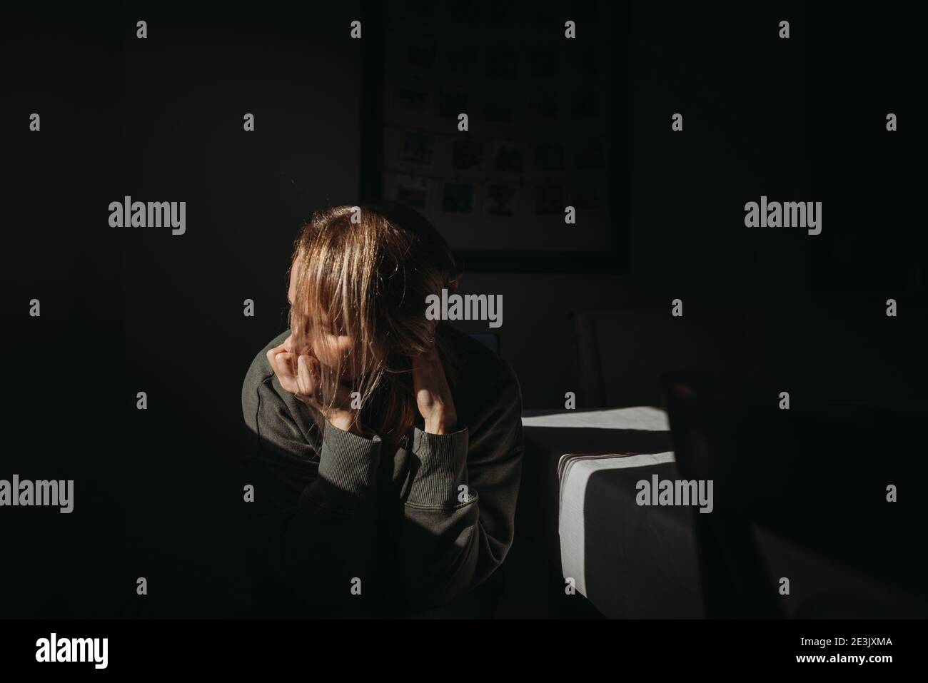 Adult woman looking distressed with face in hand with dark backdrop ...
