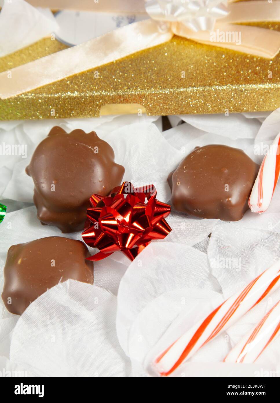 Three caramel and pecan chocolates on white petals with green and red ...