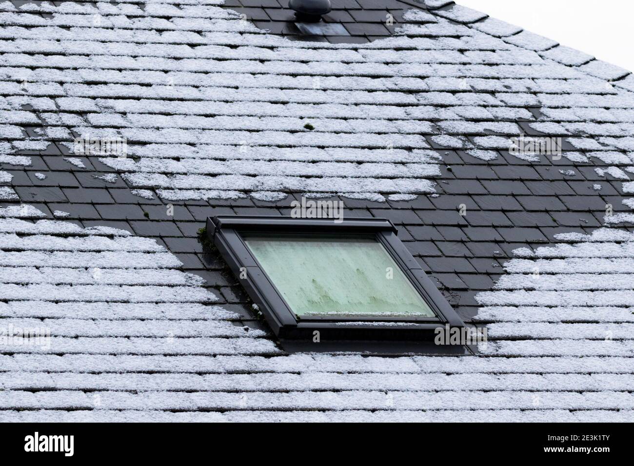 A vertical portrait of a frozen slate roof with a skylight window which ...