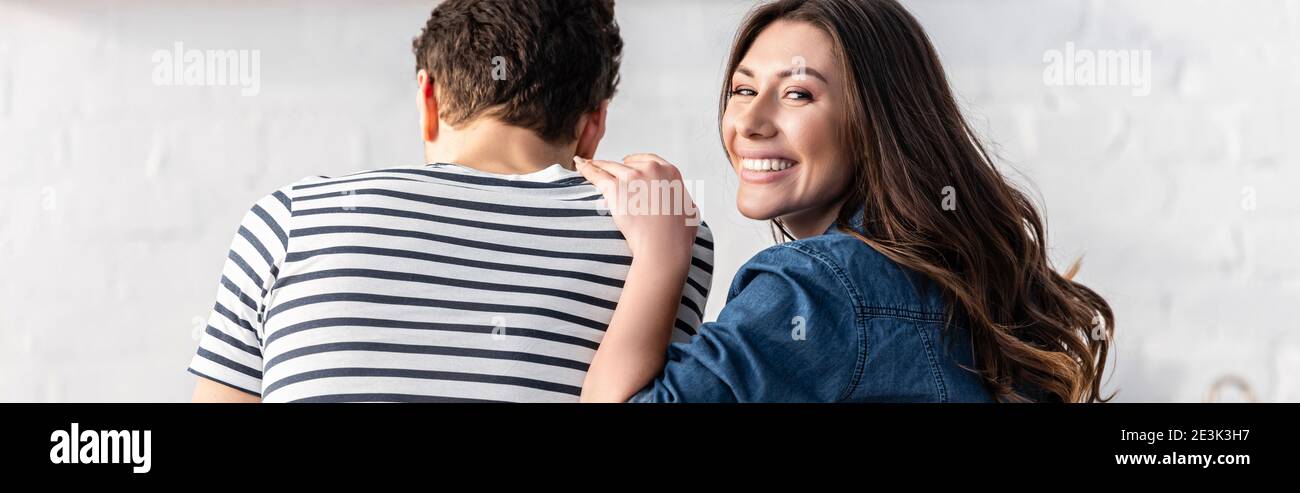 cheerful woman looking at camera while touching shoulder of boyfriend ...