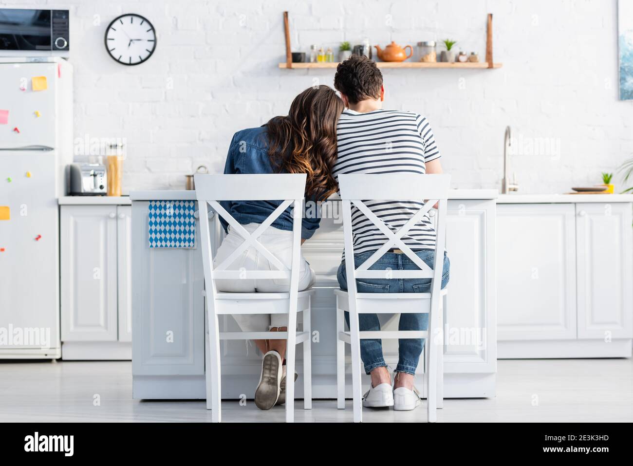 back view of man and woman sitting on chairs in kitchen Stock Photo - Alamy