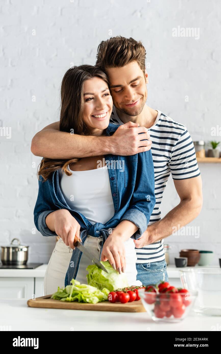 happy man hugging woman preparing salad in kitchen Stock Photo - Alamy