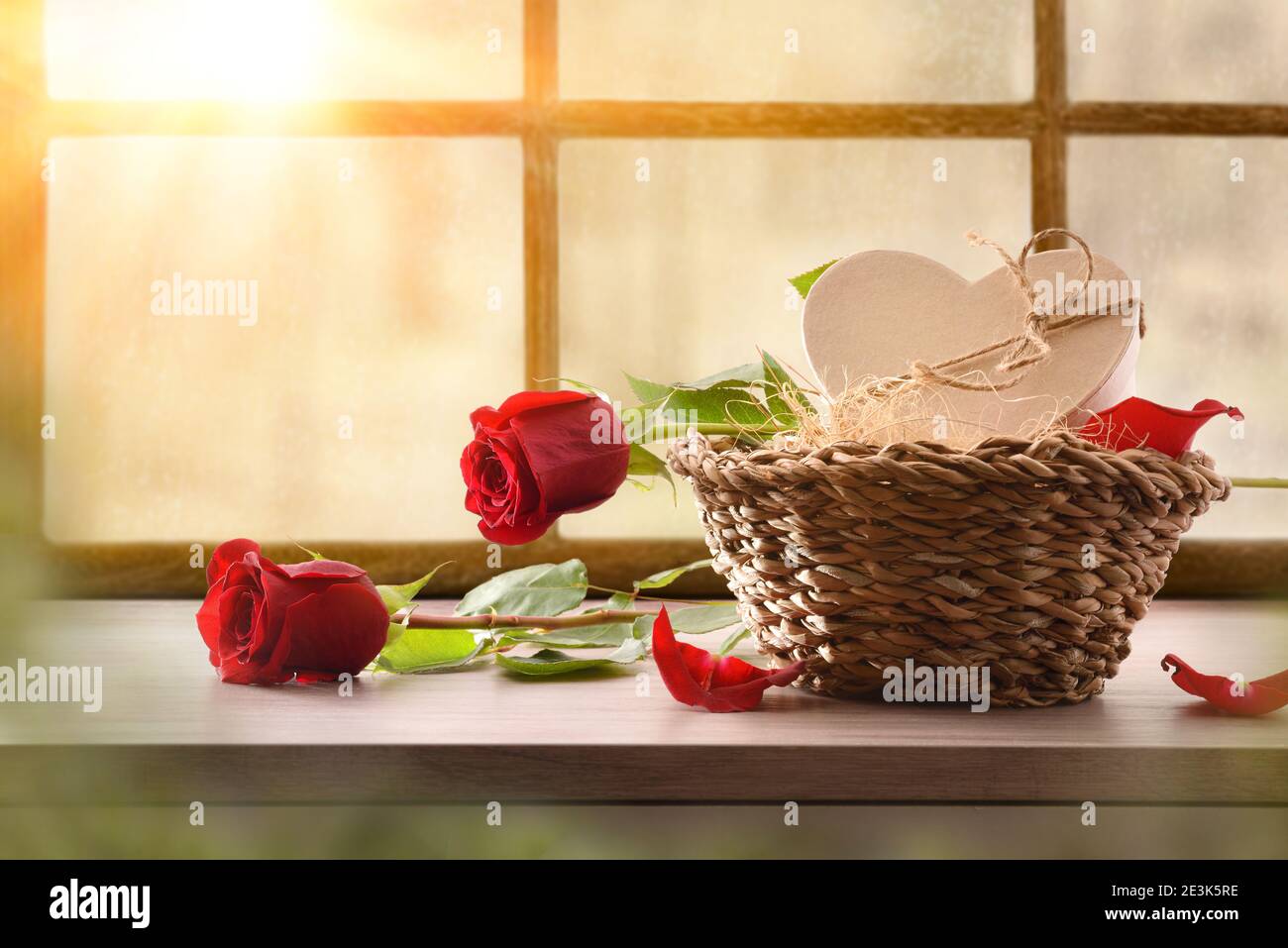 Wicker basket with gift box and red roses on interior window sill with ...