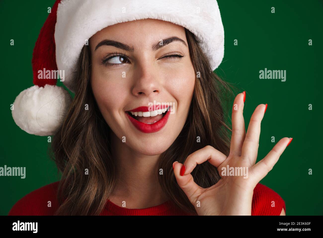 Beautiful happy girl in Santa Claus hat winking and showing ok sign ...