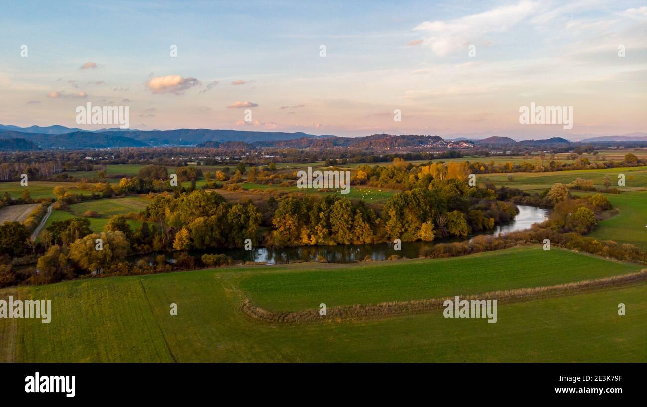 Spectacular aerial panorama of river flowing through fields at sunset ...