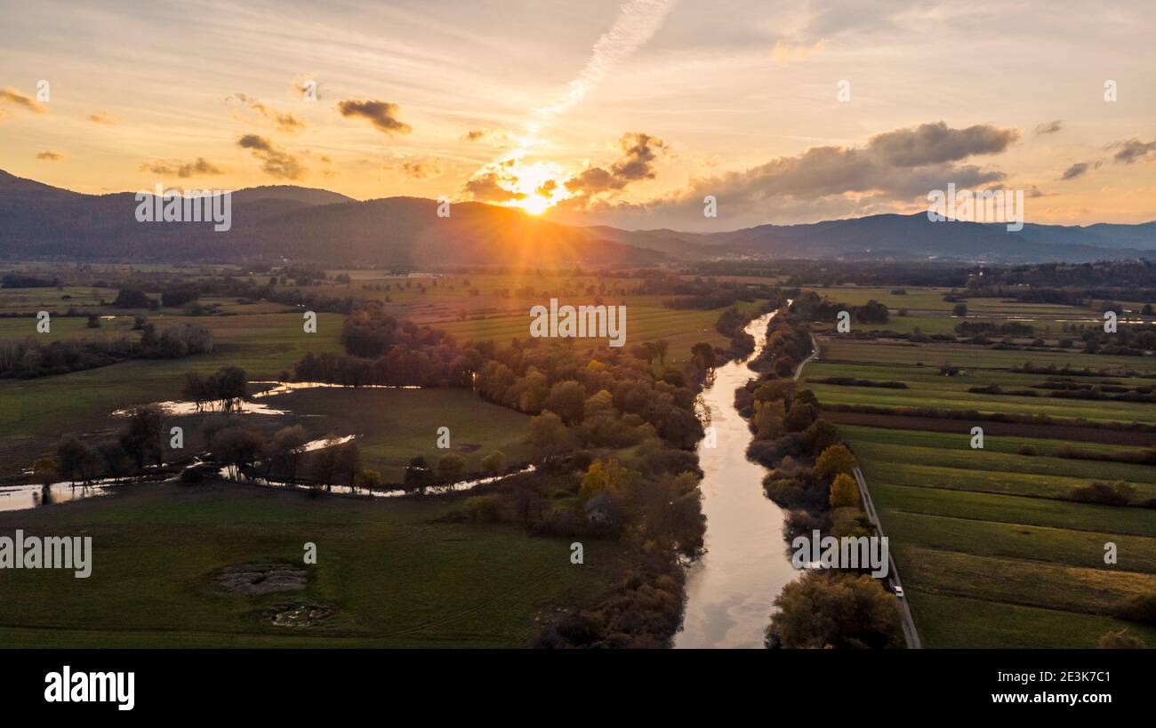 Spectacular aerial panorama of river flowing through fields at sunset ...