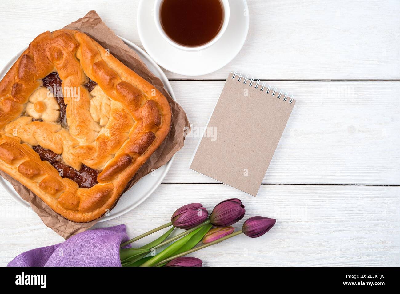 Apple pie, notepad and tulips on a light background. Top view, with ...
