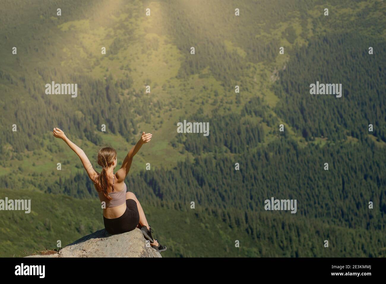 The young woman sitting at the top of the mountain raised her hands up ...