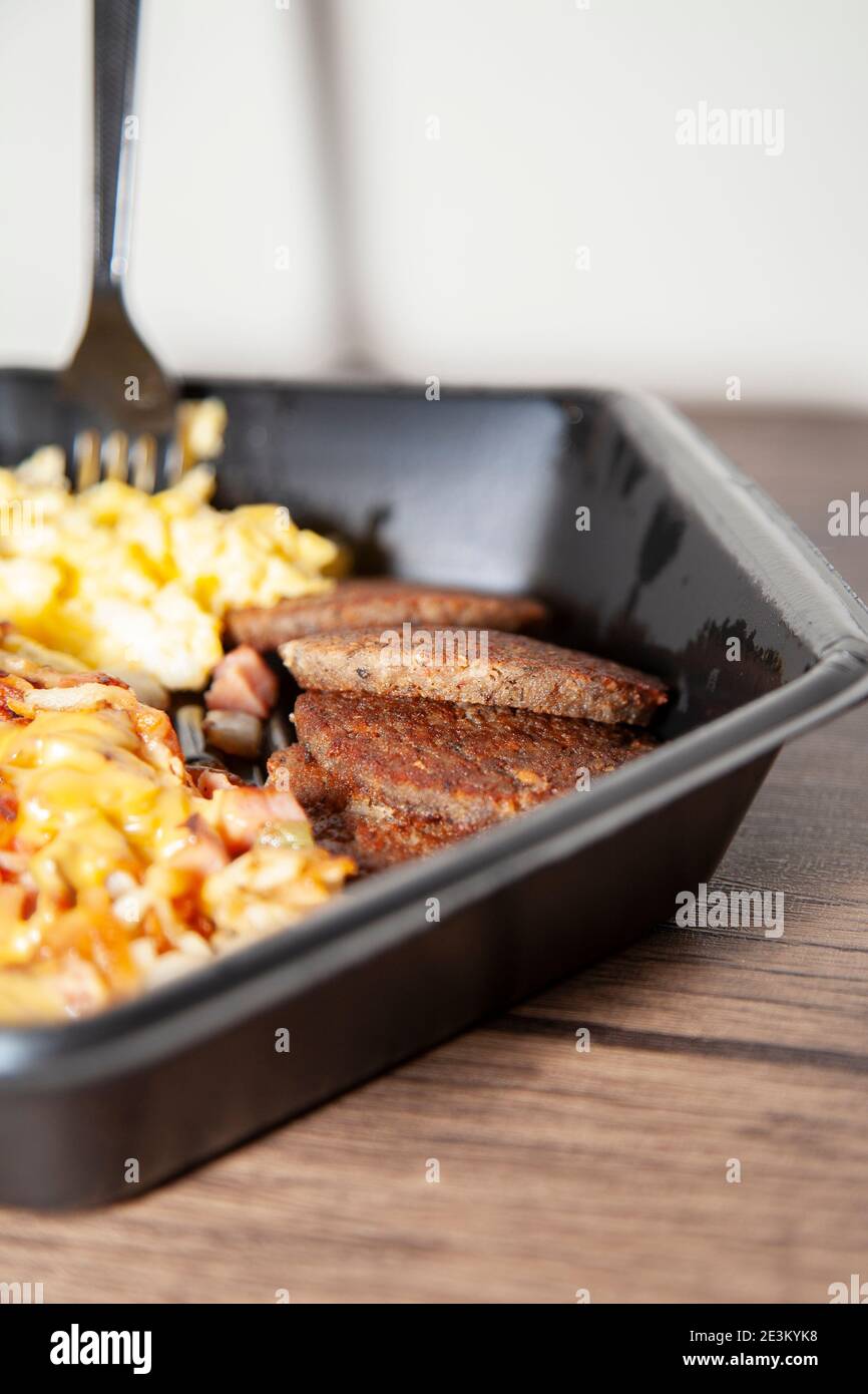 Eggs, breakfast sausage, and cheesy hash browns in a black take out ...