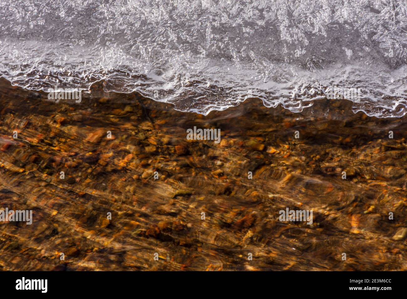 A layer of ice formed along edge of creek with fresh water flowing ...