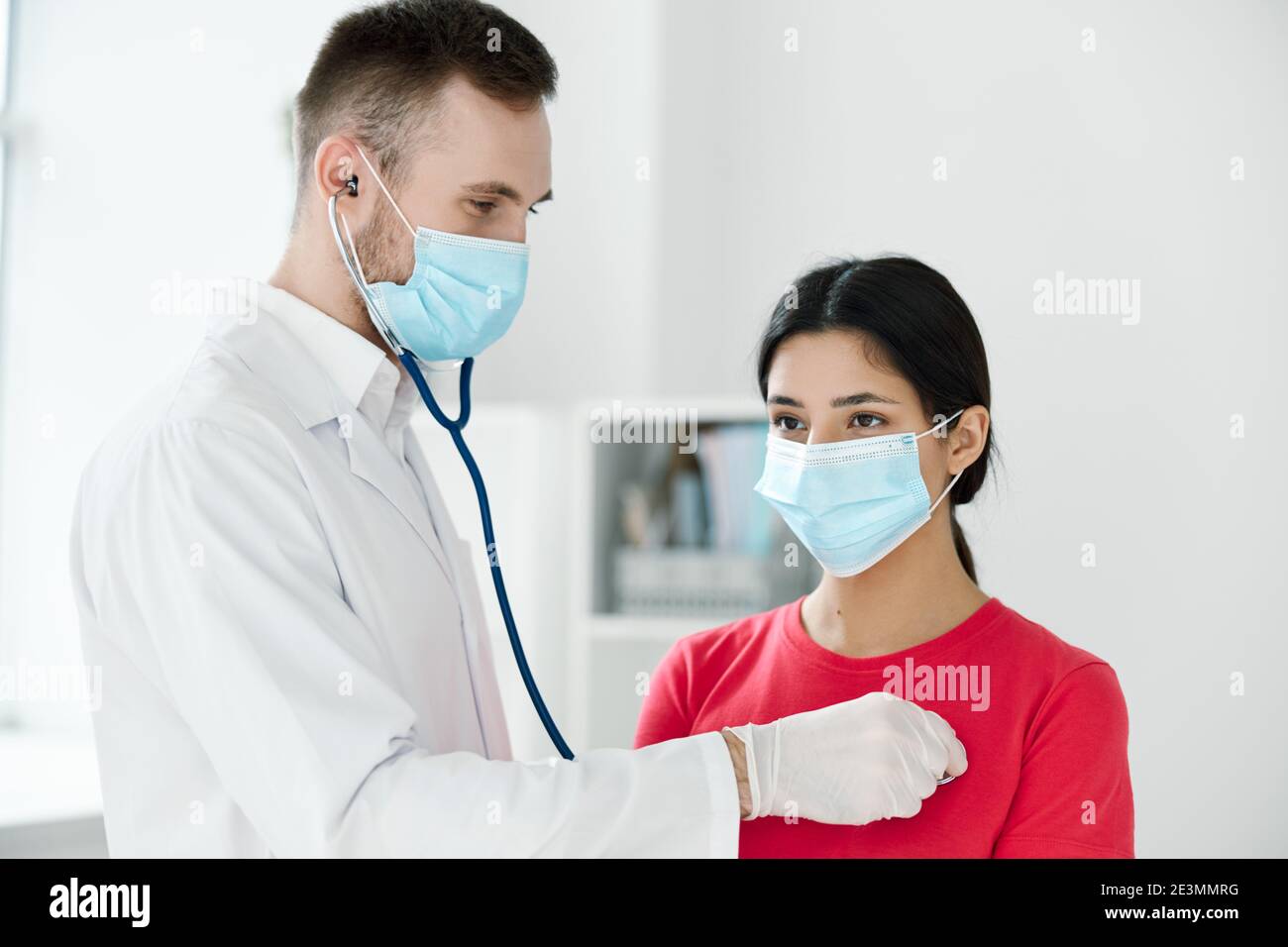 doctor with a stethoscope examines a patient wearing a medical mask ...