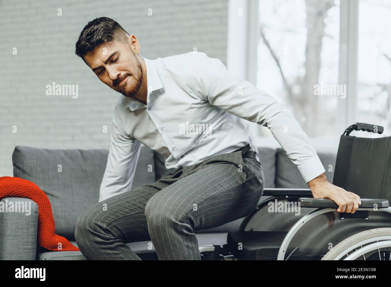 Disabled man tries to sit down on a sofa from wheelchair Stock Photo ...