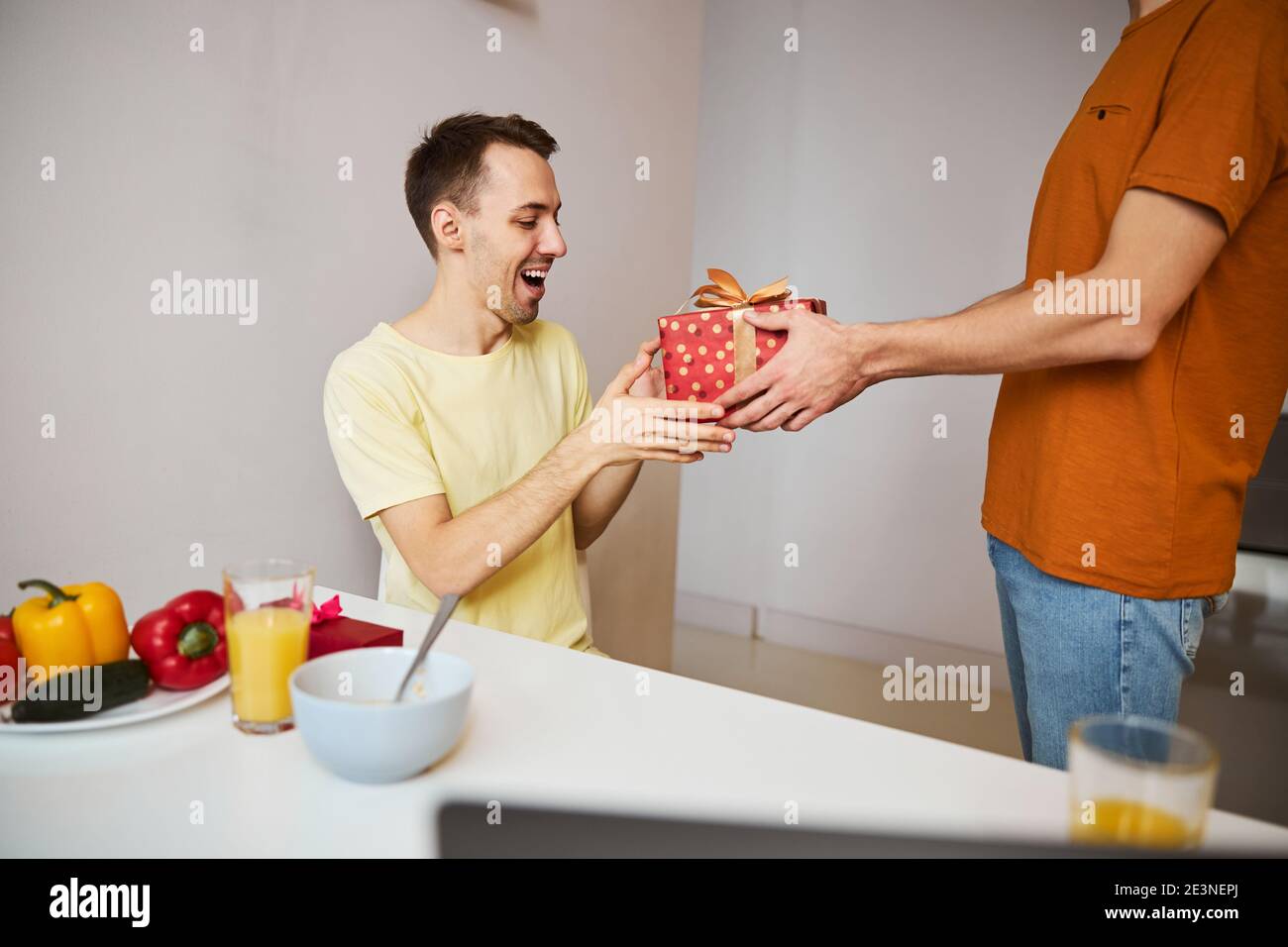 Cheerful young man accepting gift box from loving boyfriend Stock Photo ...