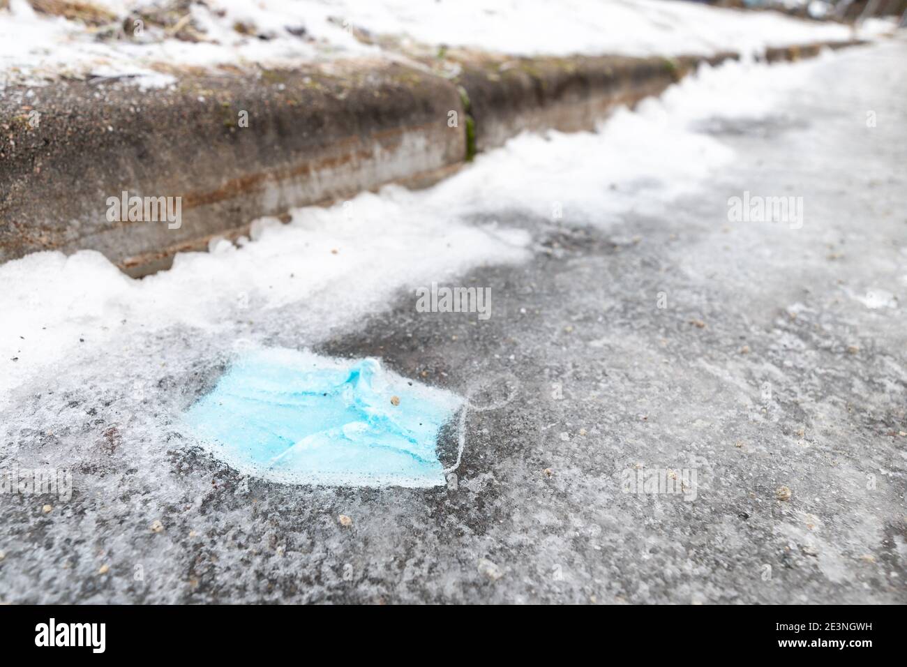 Used face mask frozen in ice on the street. Light blue surgical masks ...