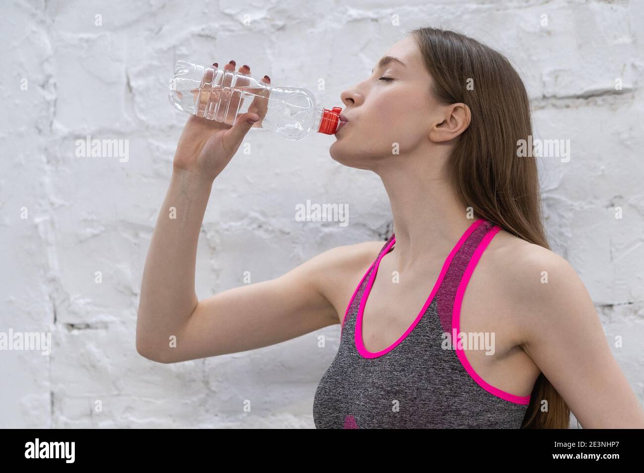 Young athlete woman takes a break drinking water from plastic bottle ...