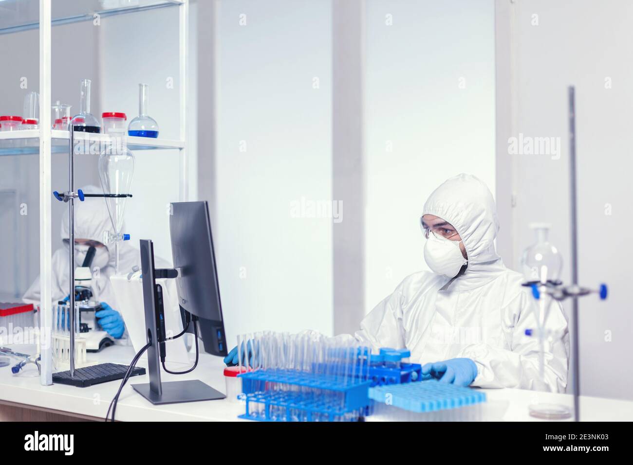 Researcher in sterile suit sitting at workplace in research laboratory ...
