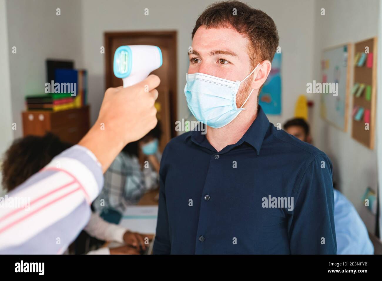 Woman worker measuring body temperature of coworker at modern office ...