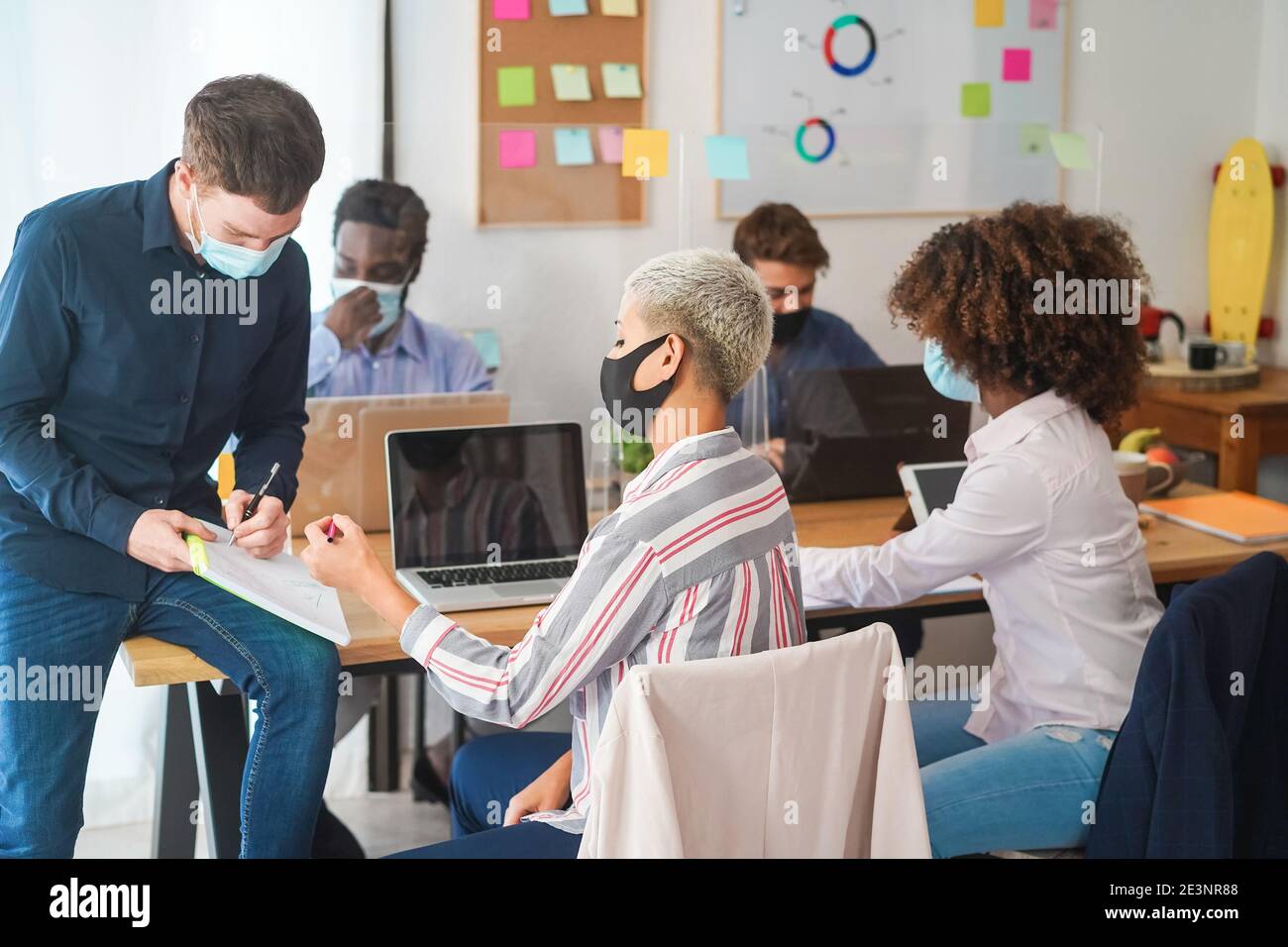 Young team working inside coworking office while wearing safety masks ...