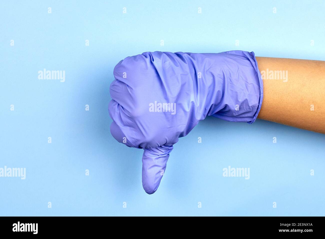 Woman's hand in a medical glove shows a thumb down gesture on a blue ...