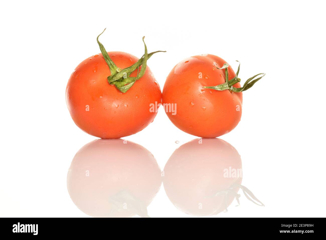 Two red round fresh juicy tomatoes with green tails, close-up, on a ...
