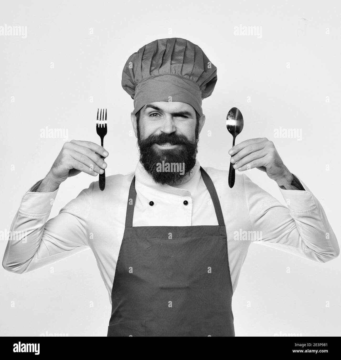 Cook with confident face in burgundy uniform shows cutlery. Chef ...