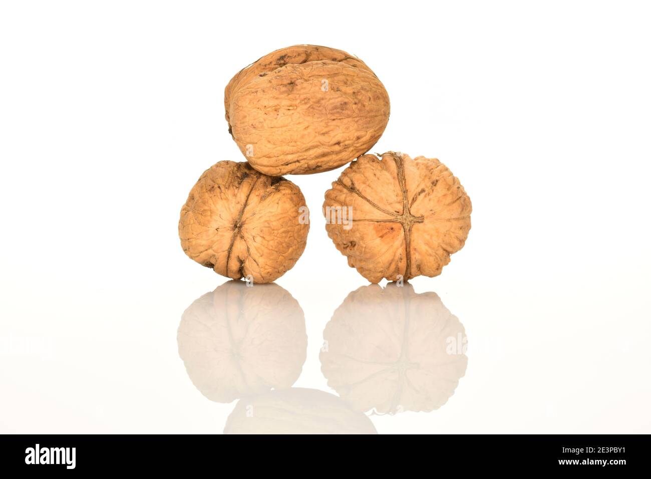 Three whole dark brown ripe natural walnuts, on a white background. On ...