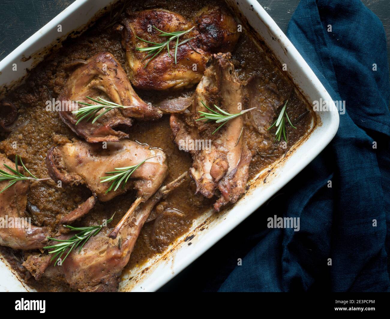 Roasted rabbit with rosemary in white pan on dark background. Dark and ...