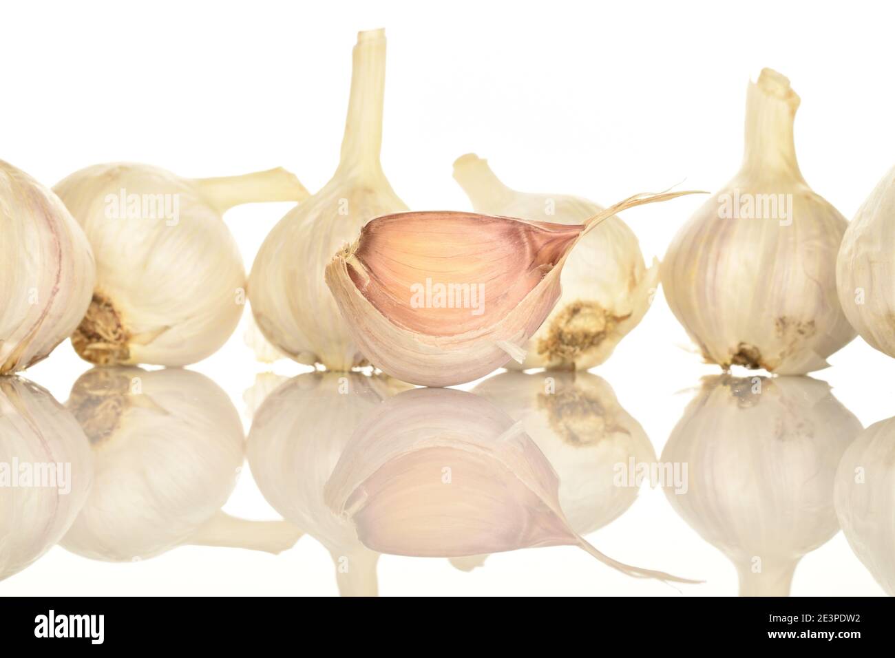 One clove of garlic in the foreground, in focus. A few whole heads of ...