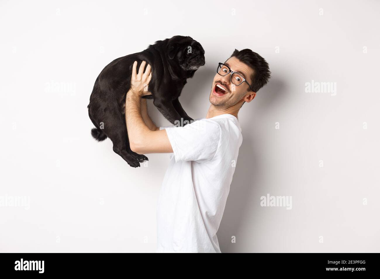 Image of handsome young man loving his pug. Dog owner holding puppy and ...