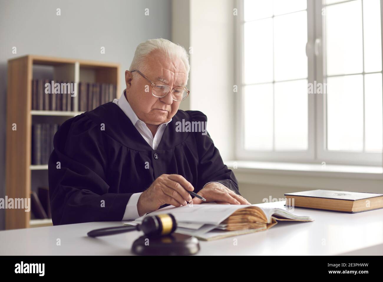 Serious wise mature judge in gown sitting at desk in courtroom and ...