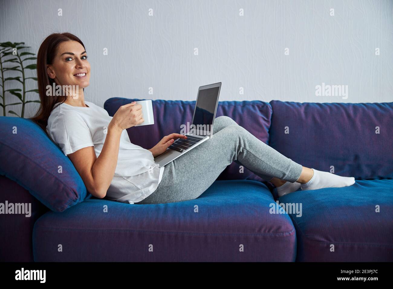 Relaxed woman with hot drink and laptop indoors Stock Photo - Alamy