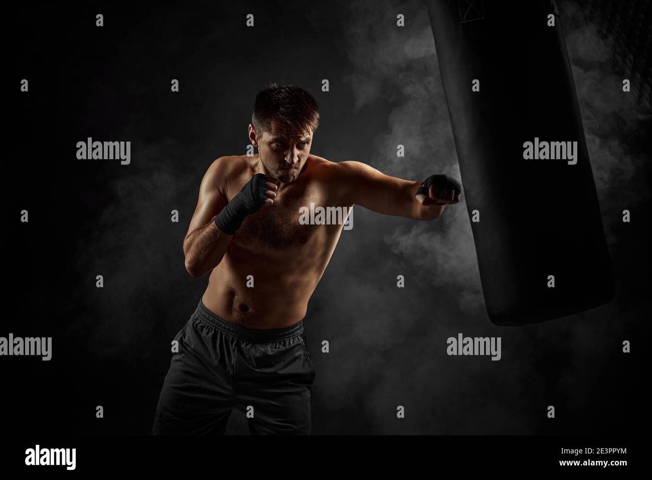Male boxer training defense and attacks in boxing bag on black ...