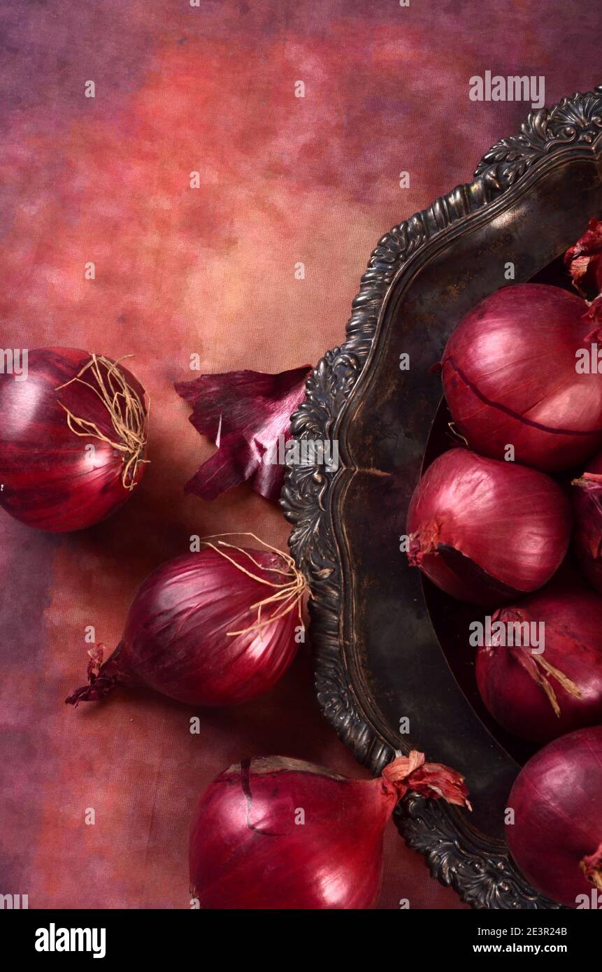 Several red onions on a metal plate, purple background. Still life with ...