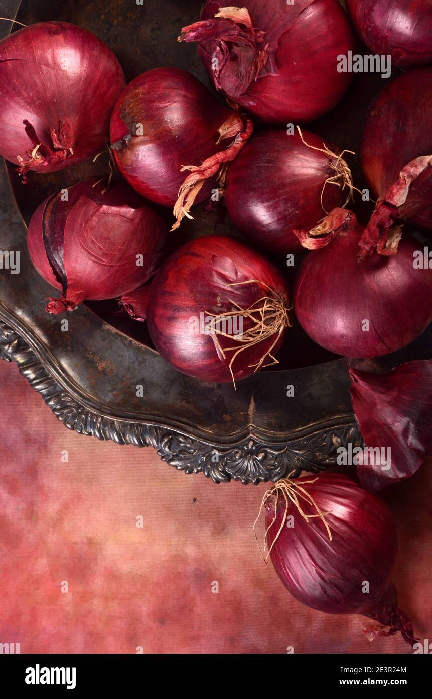 Several red onions on a metal plate, purple background. Still life with ...