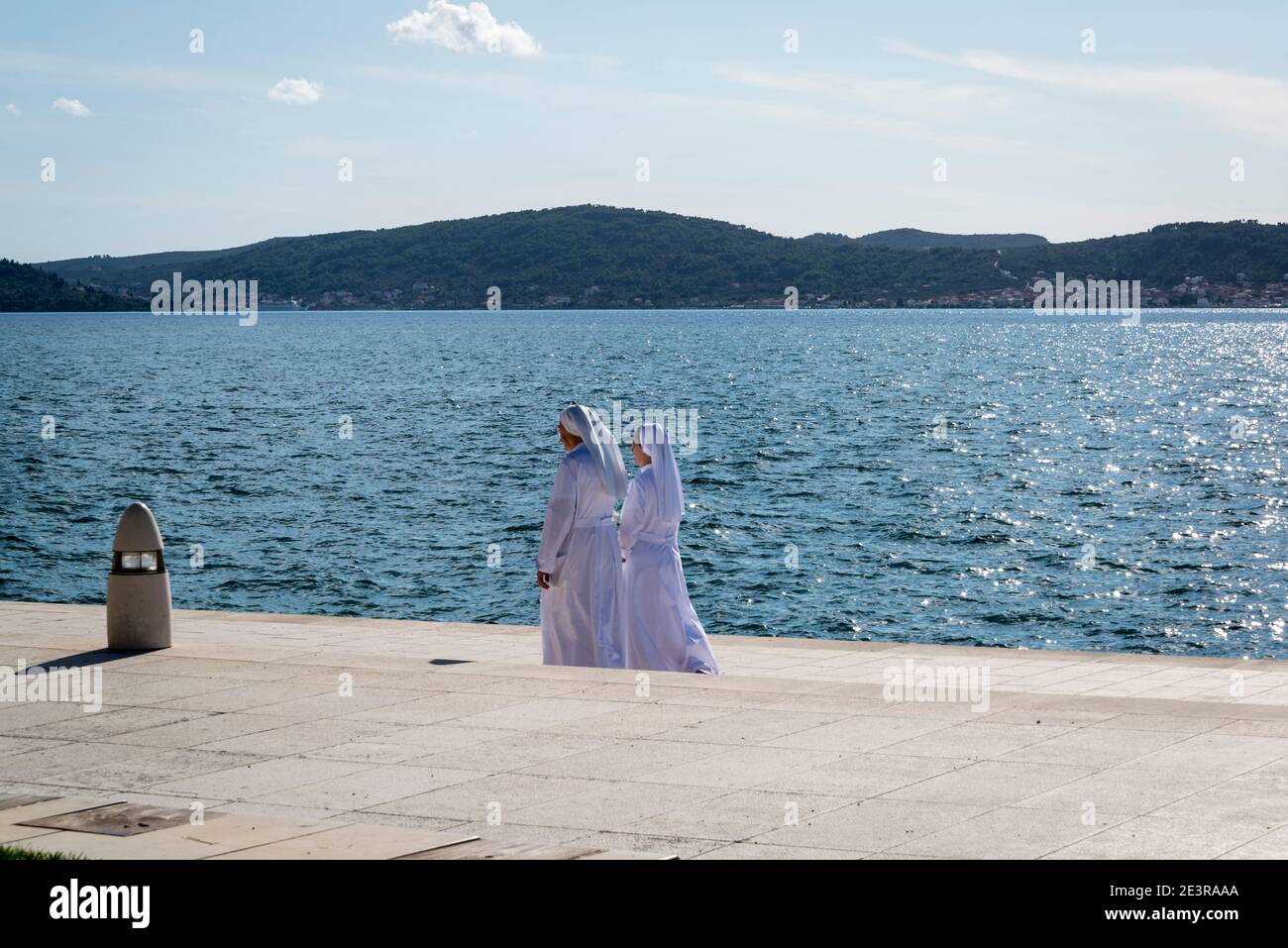 Two Roman Catholic nuns dressed in white clothes walking on the Seaside ...