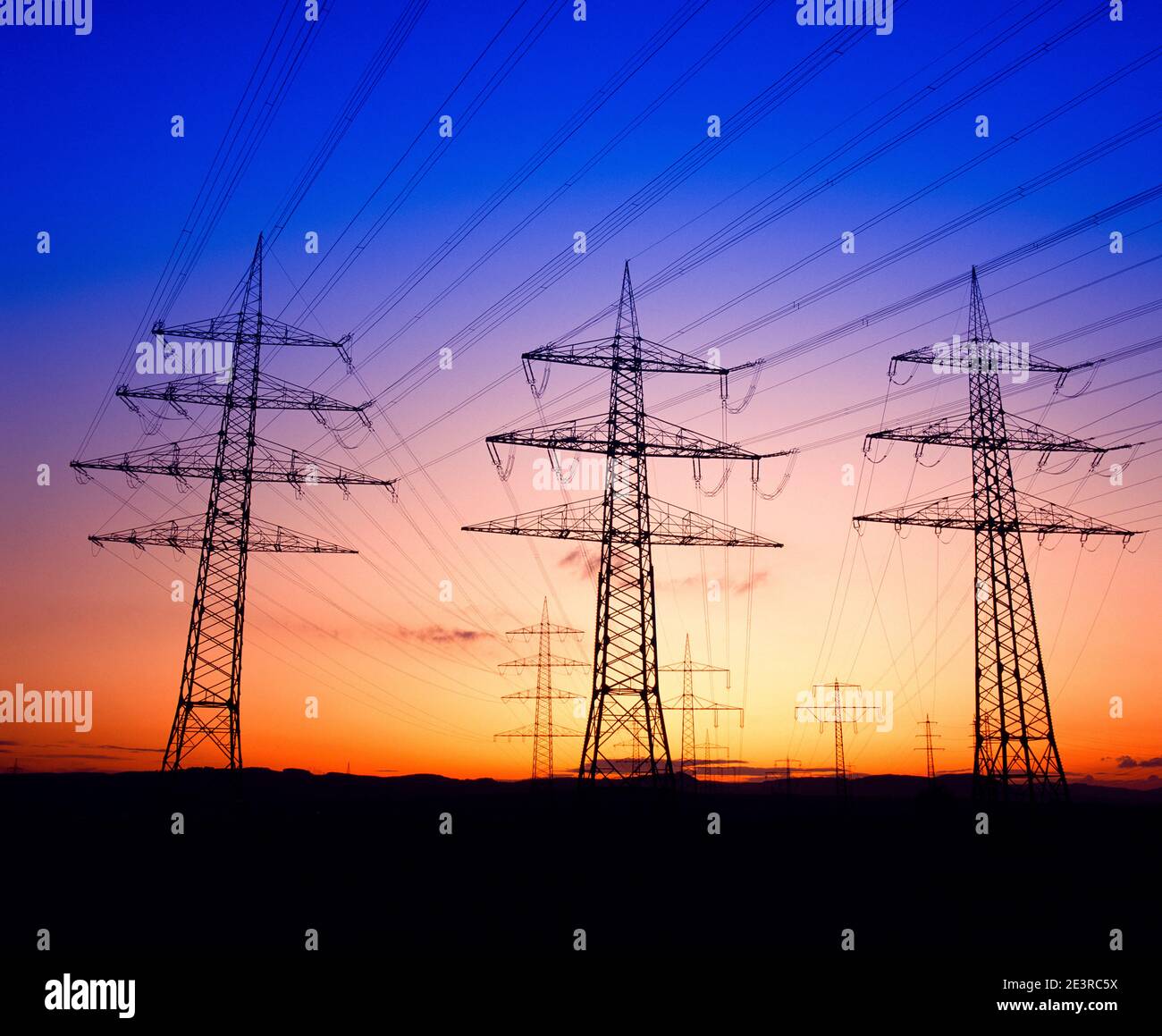 Electric electricity pylons, transmission towers silhouetted at sunset ...