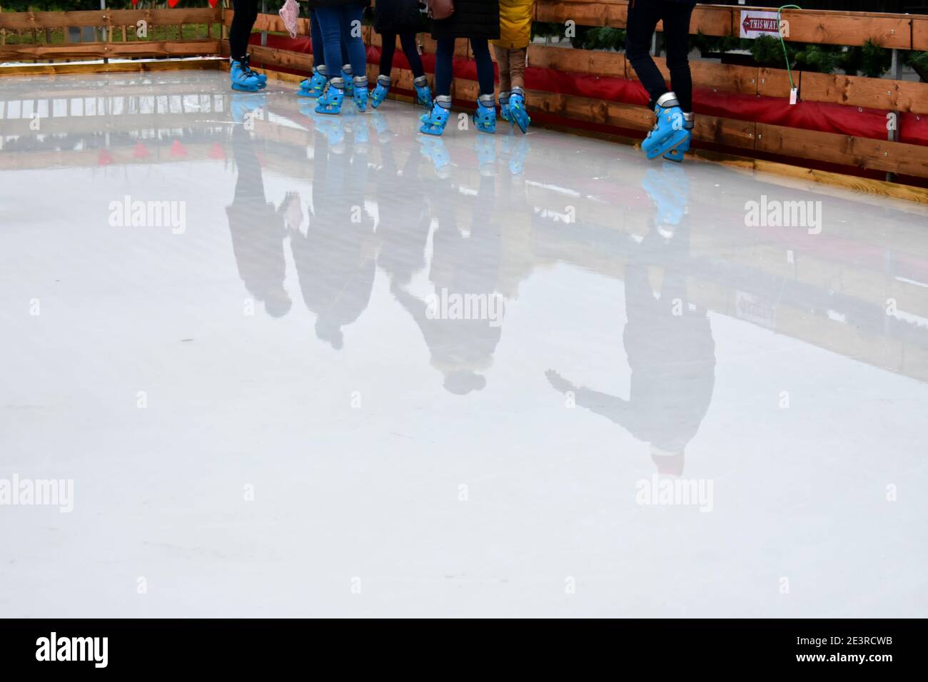 Reflection of family of ice skaters and their feet on outdoor ice rink ...