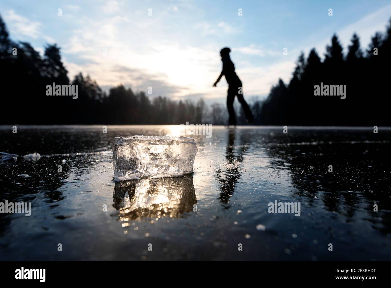 A clear cube of ice and its reflection on flat frozen lake, at sunrise ...