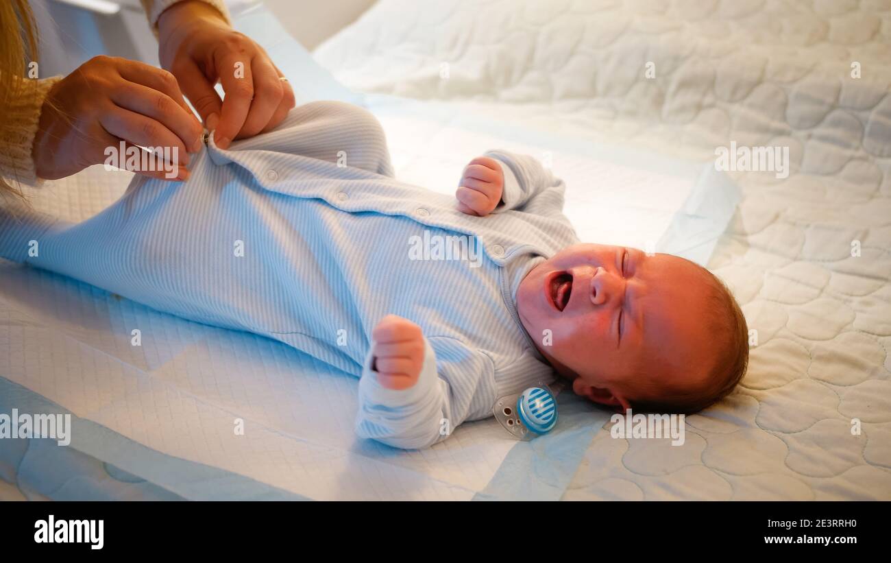 Little newborn baby getting dressed and sucking pacifier on bed at ...