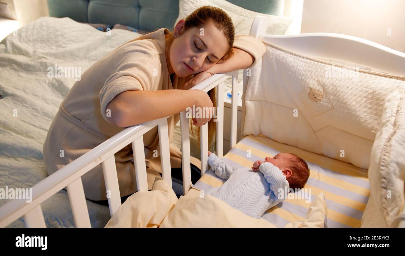 Young tired and exhausted mother fallen asleep while rocking crib of ...