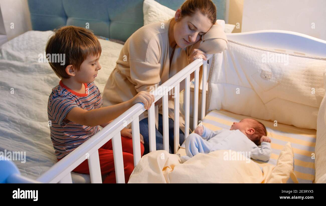Older boy helping his tired mother rocking baby ccrib in bedroom at ...