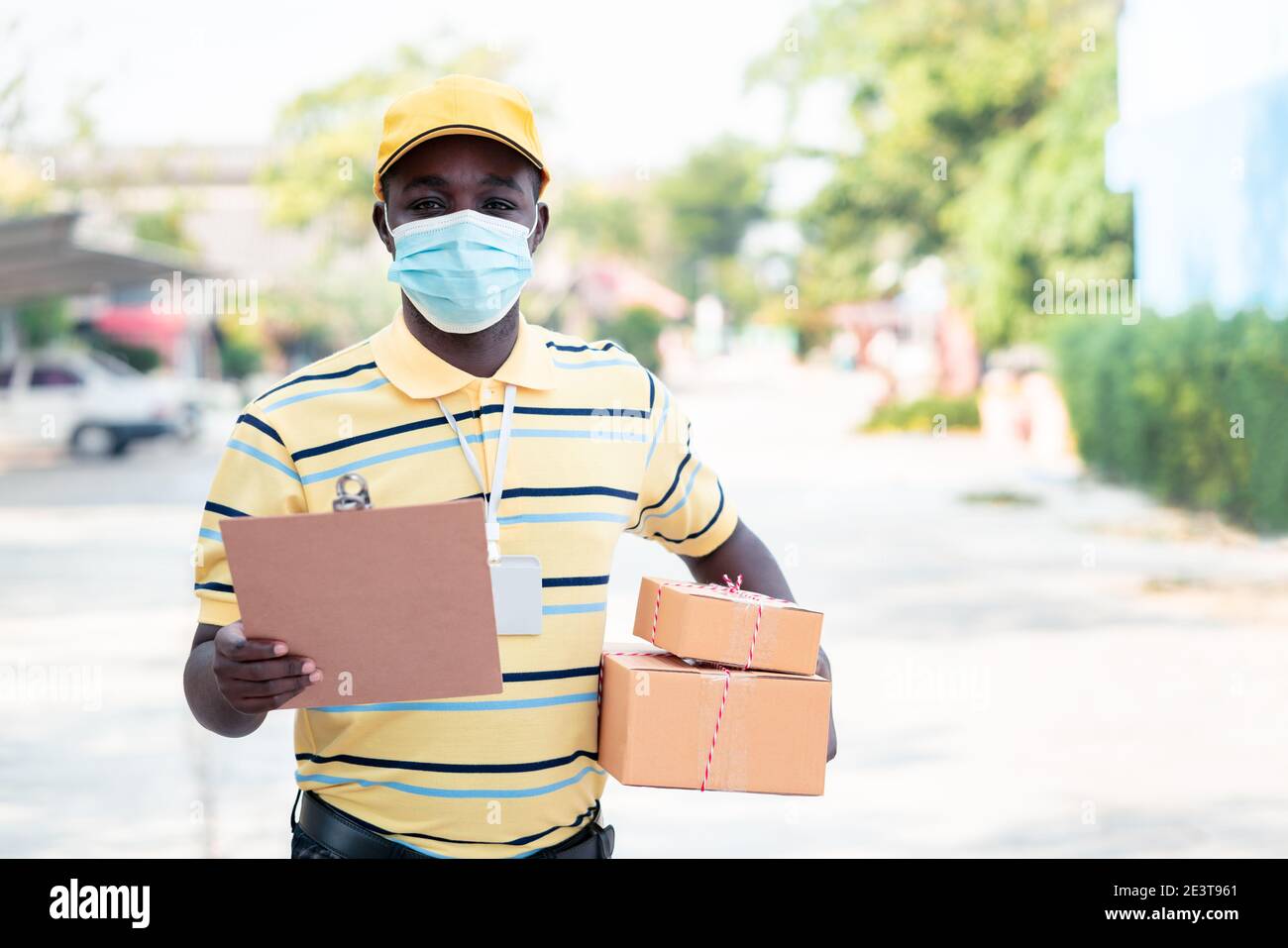 African delivery man holding boxs and cardboard with wearing face mask ...