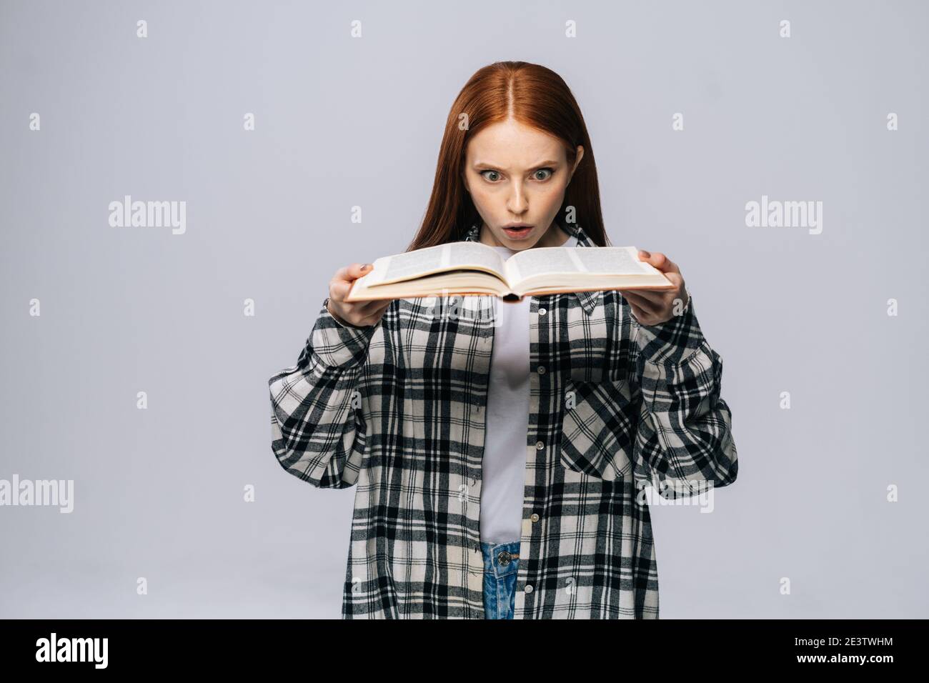 Shocked young woman college student reading book on gray isolated ...