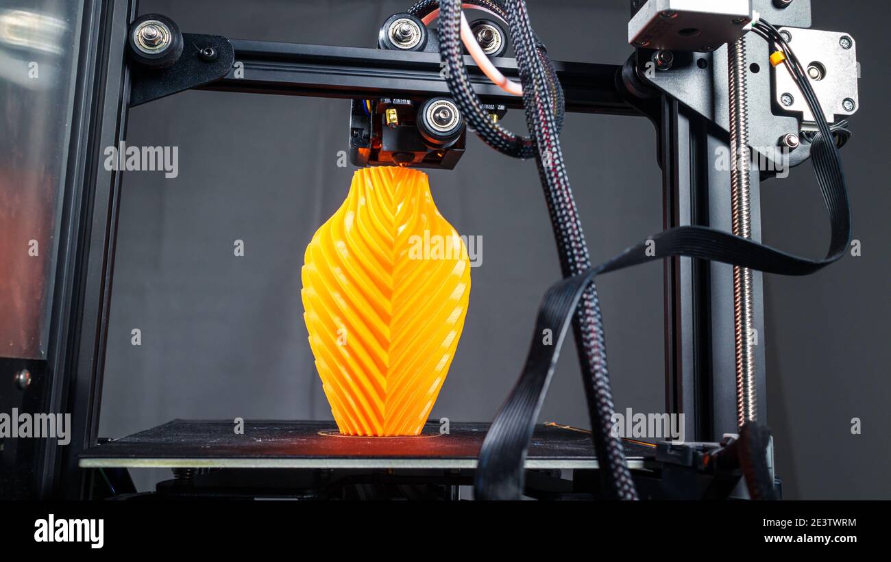 3D Printer printing a vase for home decoration with orange plastic ...