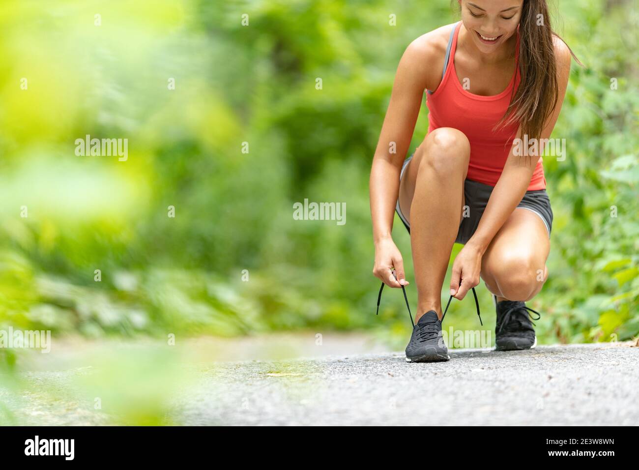 Fitness girl getting ready to run exercise outside lacing running shoes on run path in forest ...