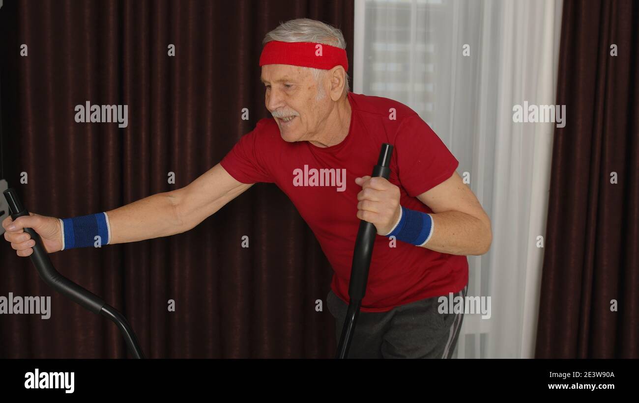 Old grey-haired senior grandfather model exercising workout on orbitrek ...